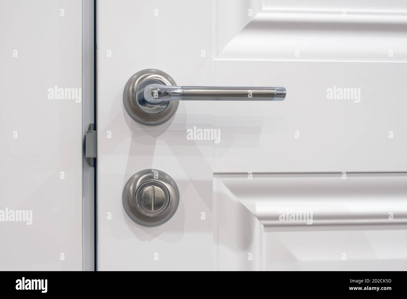 Metal handle with a rotary lock on a white half-open door, close-up ...