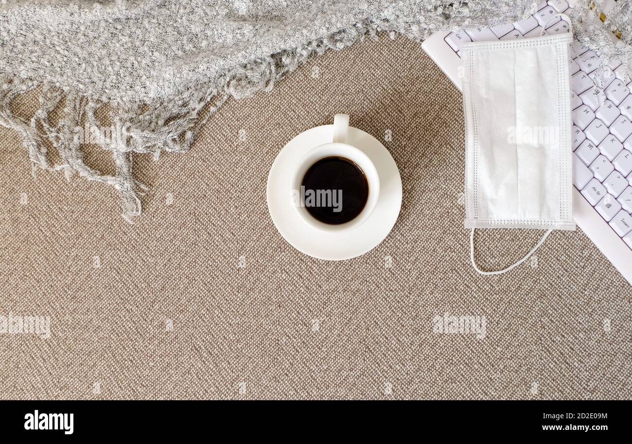 A cup of coffee, a keyboard, plaid and a medical mask are on the sofa ...