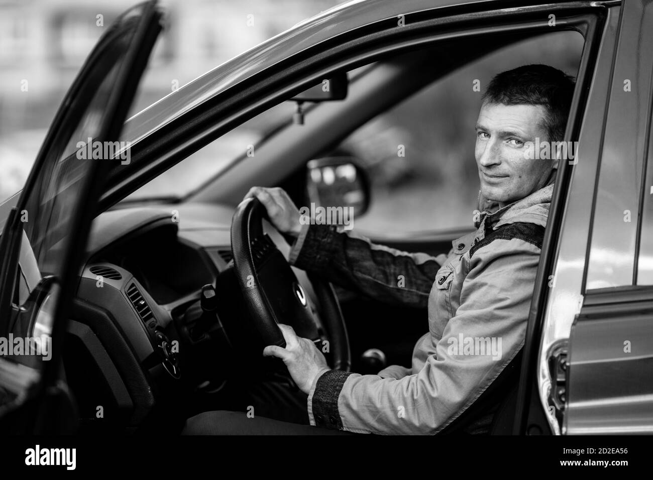 Happy man sits behind the wheel of a car. Black and white photography ...
