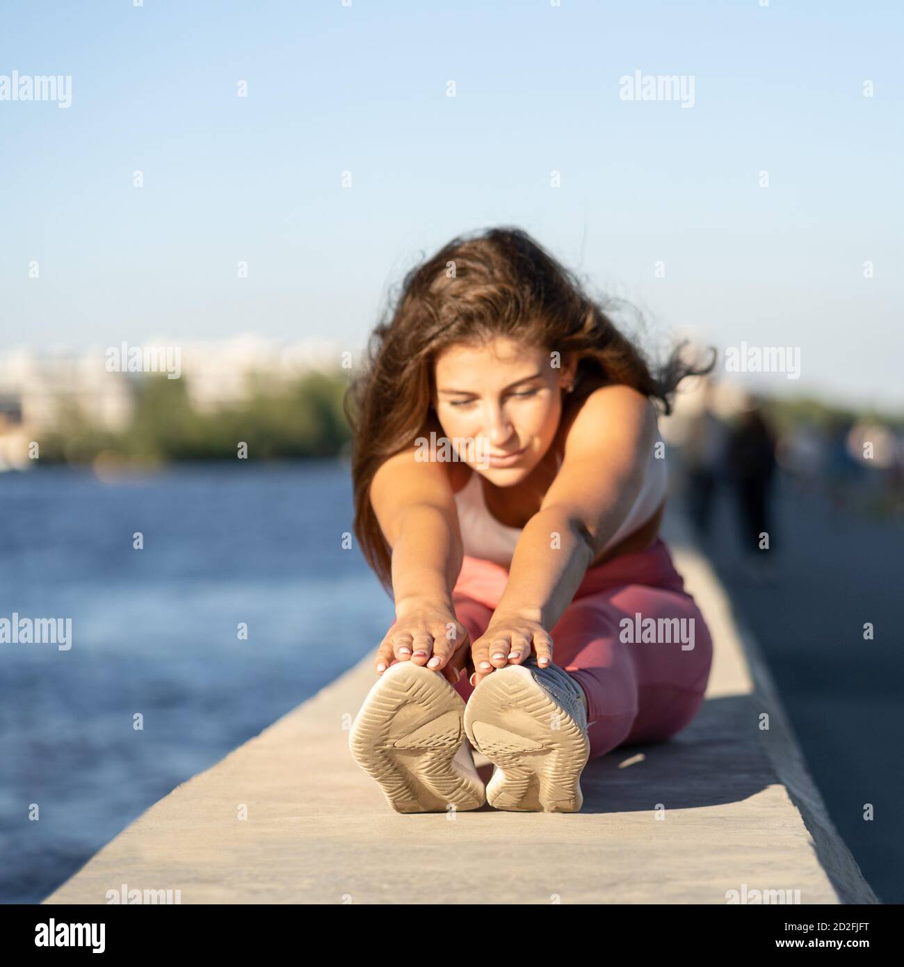 Young fit woman in pink legging sitting on embankment, stretching ...