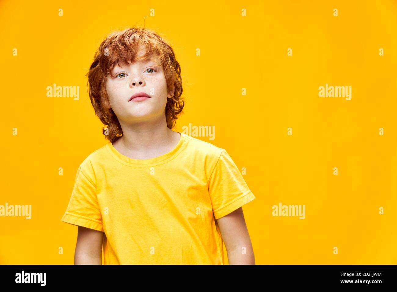 Red-haired child front view in a yellow t-shirt interested facial ...