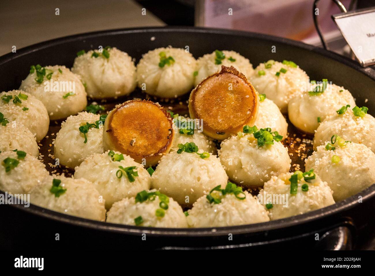 a pan of pan fried chinese buns with spring onion and sesame seeds on ...