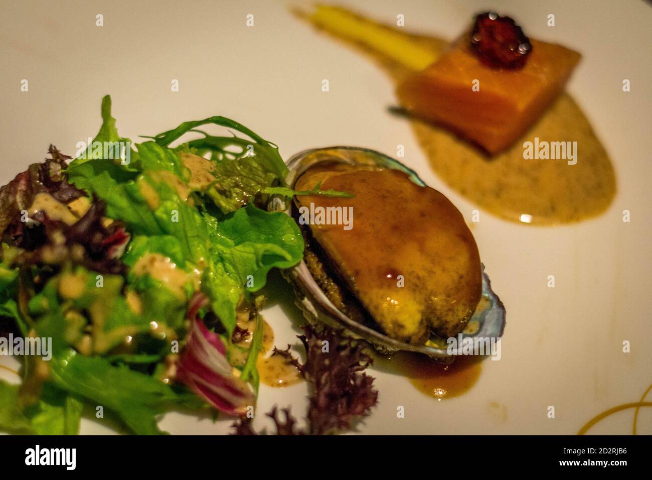 an appetizer of briased abalone and salmon cube with salad on the side ...