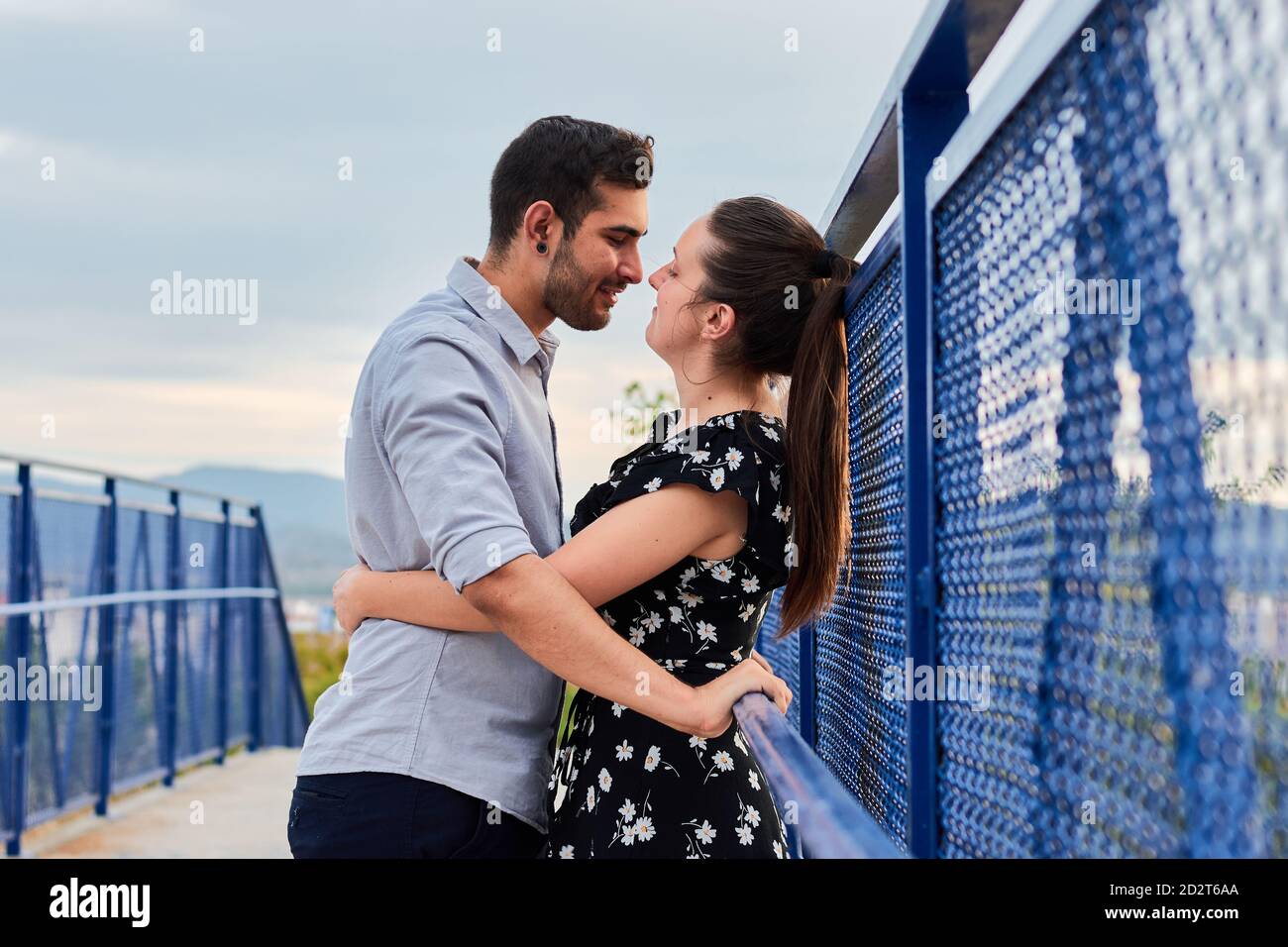 Side view of romantic couple standing on bridge and tenderly cuddling ...