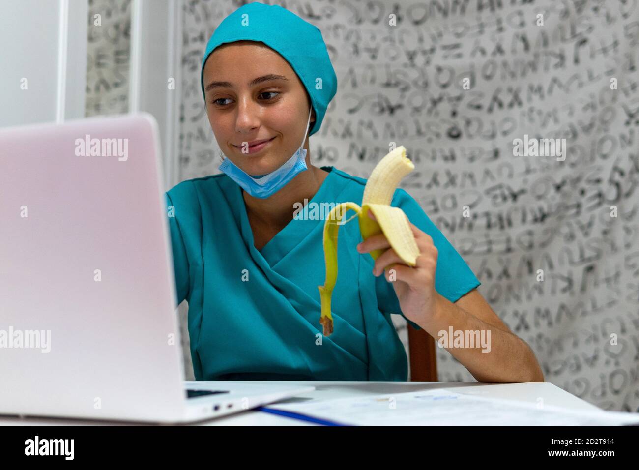 Positive young female medical worker in blue uniform using laptop and ...
