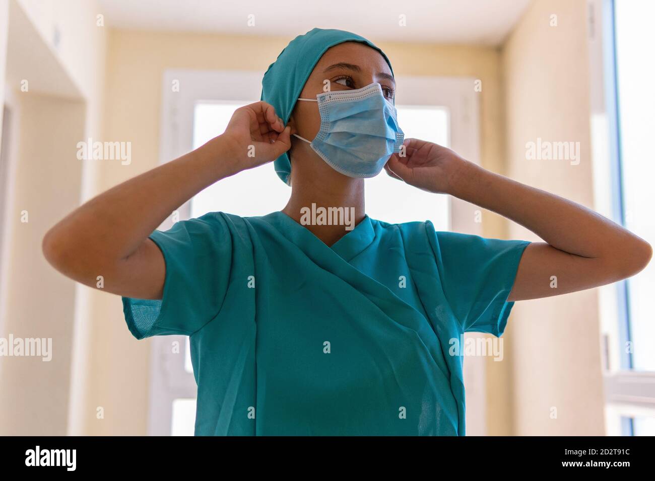 Serious female nurse in uniform putting on medical mask before work ...