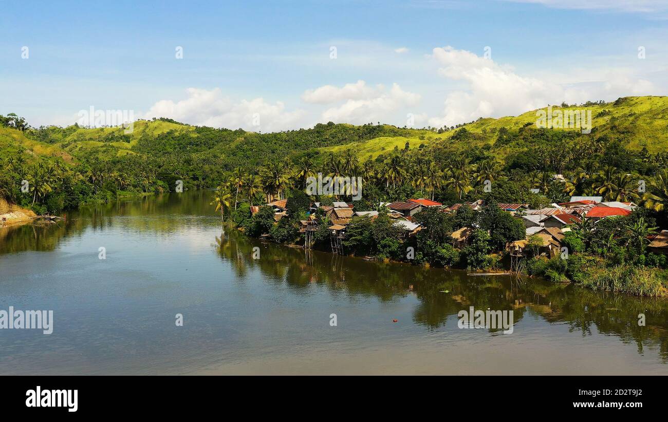 Tropical landscape in sunny weather. Village by the river. Green hills ...