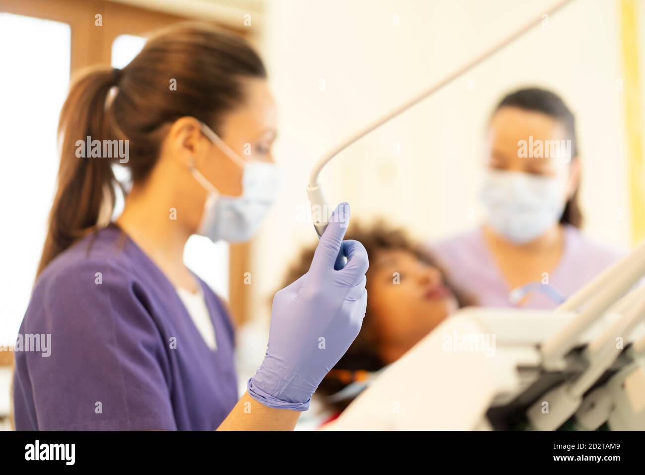 Female dentist in uniform taking dental drill from stand on blurred ...