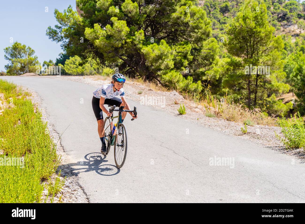 Full length of strong female bicyclist riding bike on curvy paved road ...
