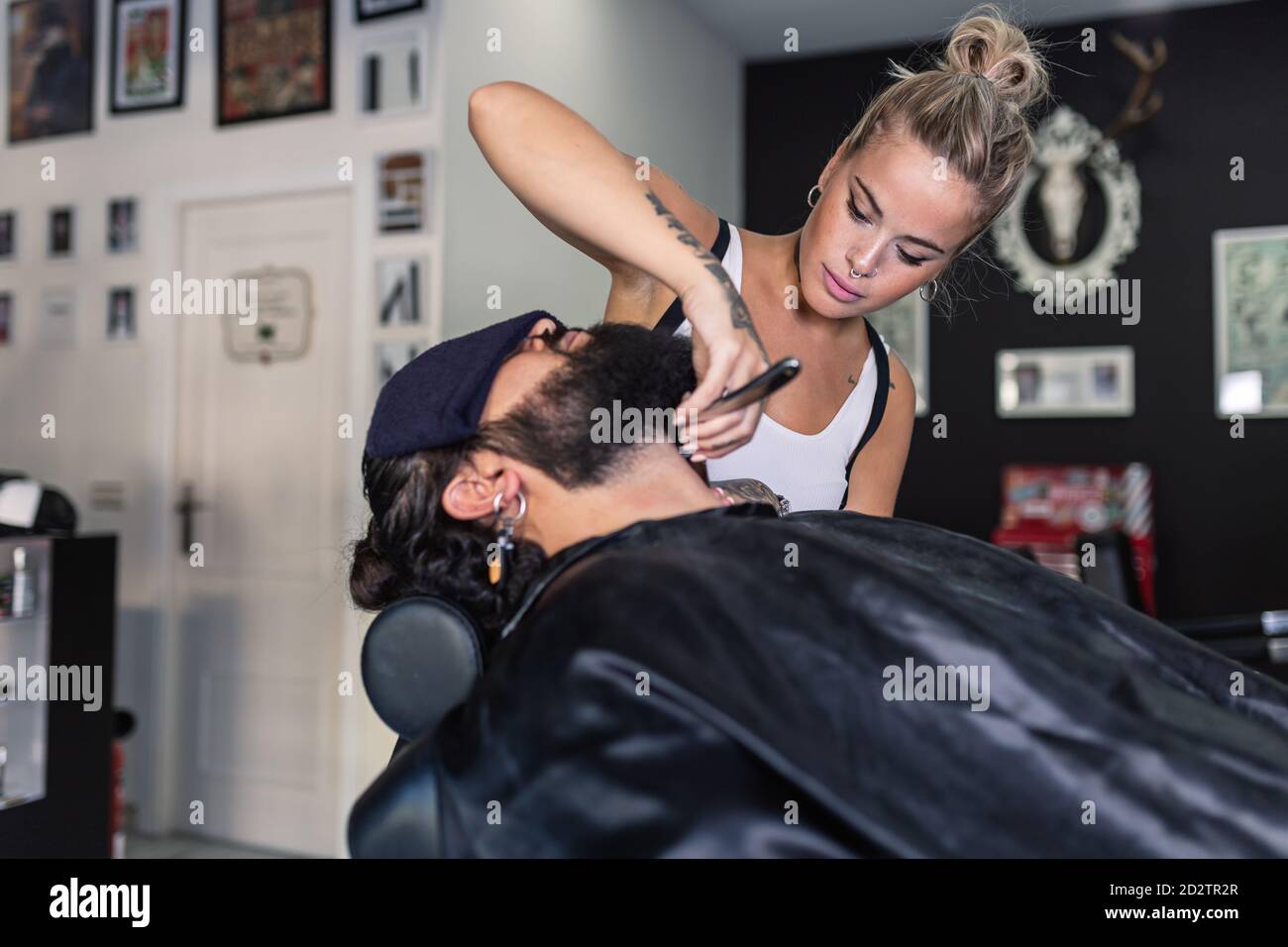 Side view of stylish tattooed female master shaving bearded customer ...