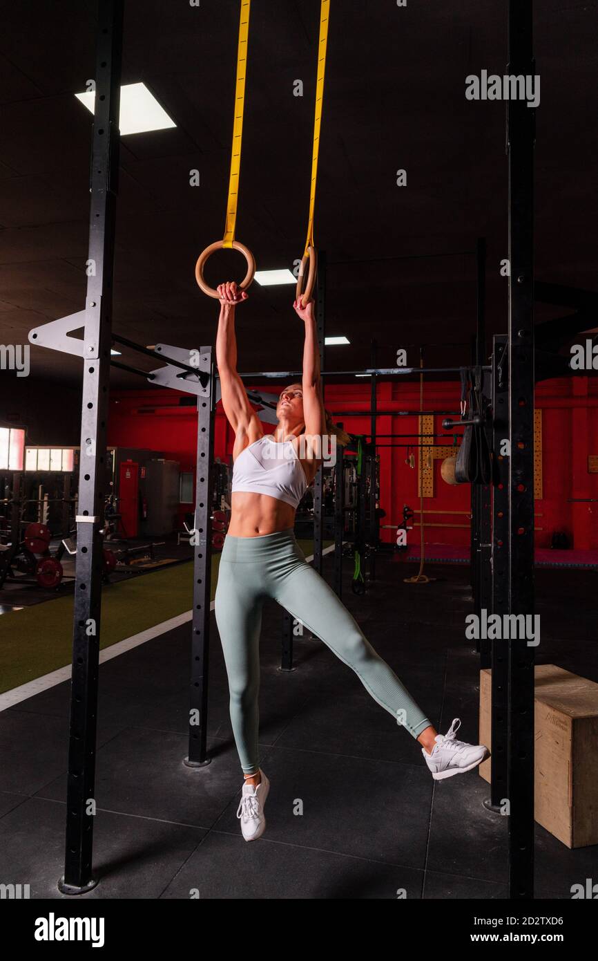 Muscular female athlete in sportswear hanging on gymnastic rings and ...