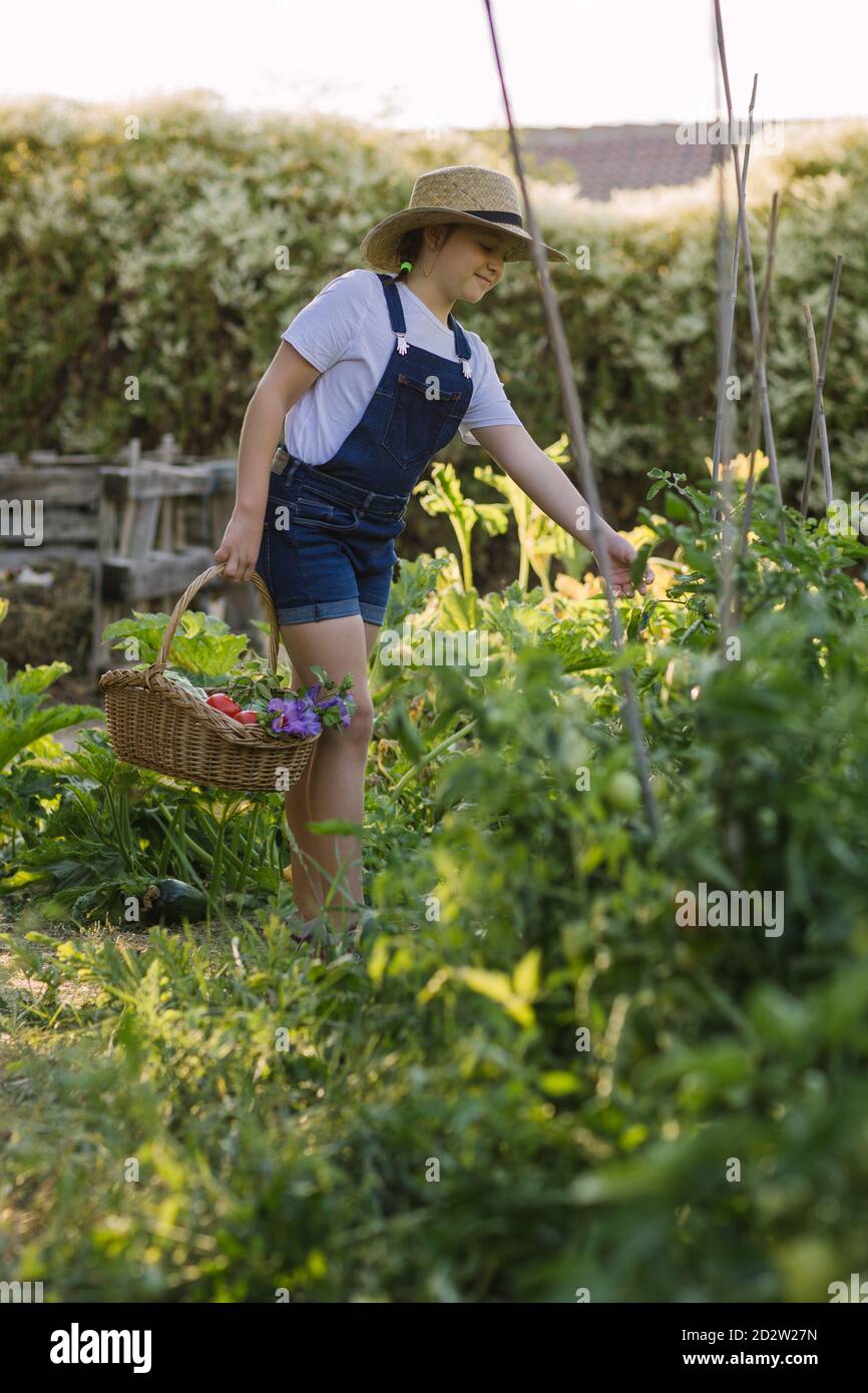 Side view of cute kid in straw hat standing in lush garden and ...