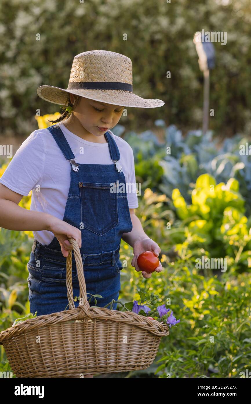 Side view of cute kid in straw hat standing in lush garden and ...