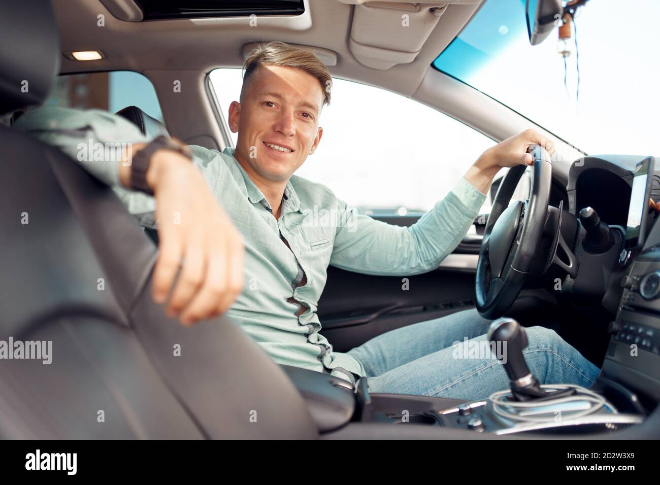 Side view of handsome smiling male driver sitting in parked luxury car ...