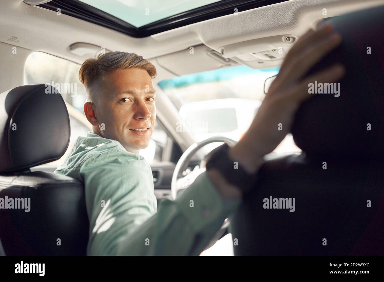 Side view of handsome smiling male driver sitting in parked luxury car ...