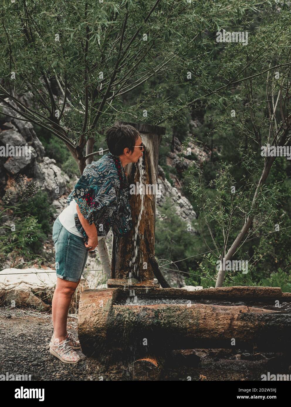 Elderly woman by the spring in the nature. Senior woman drinking water ...