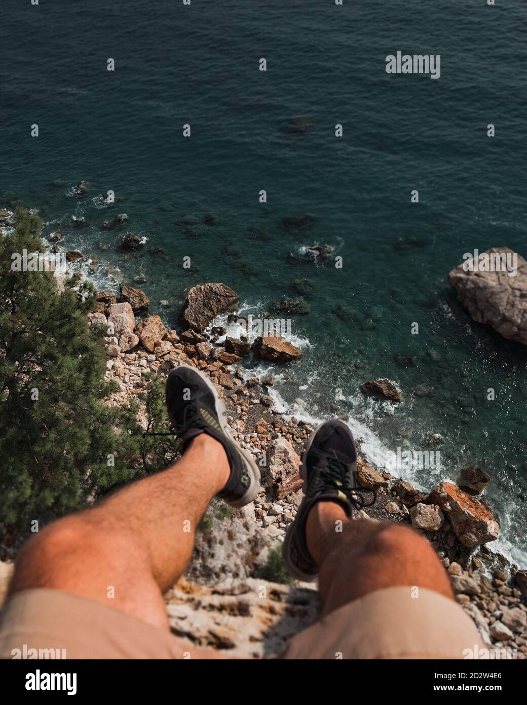Legs of man are hanging from edge of cliff over the sea and rocks Stock ...