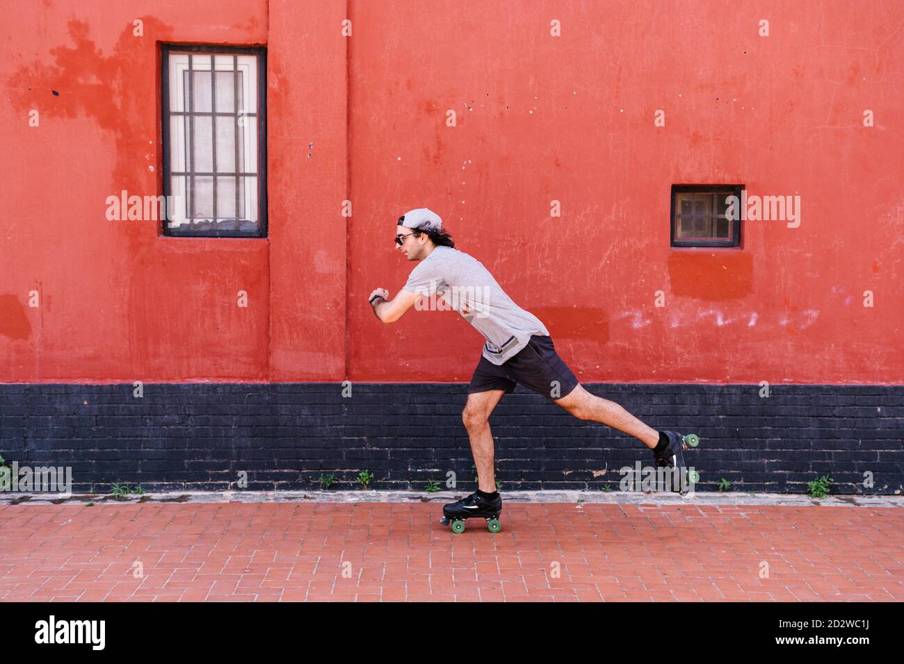 Side view of active stylish male in roller skates skating along street ...