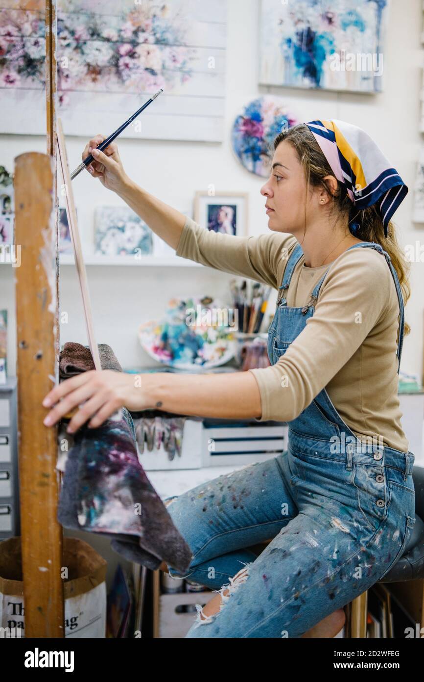 Side view of female artist sitting near easel and drawing colorful ...