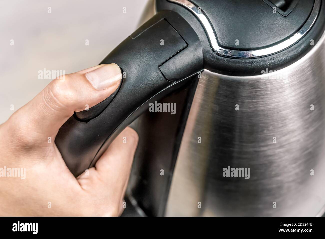 woman's hand holds the black handle of a gray electric kettle and ...