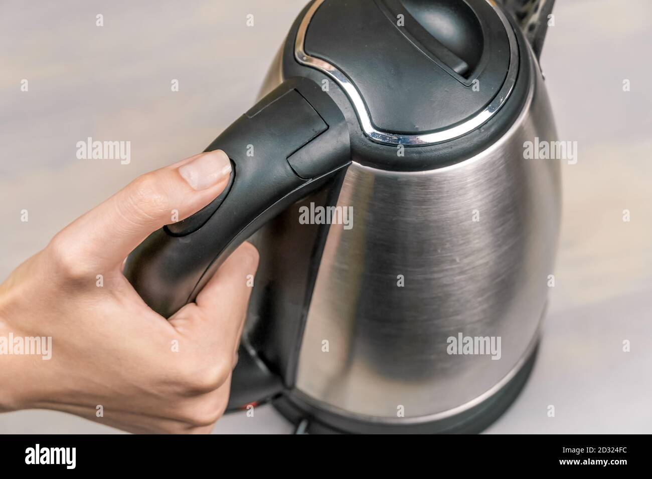 woman's hand holds the black handle of a gray electric kettle and ...