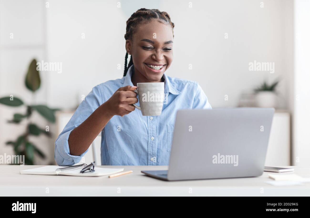 Cheerful Black Female Office Worker Using Laptop And Drinking Coffee At ...