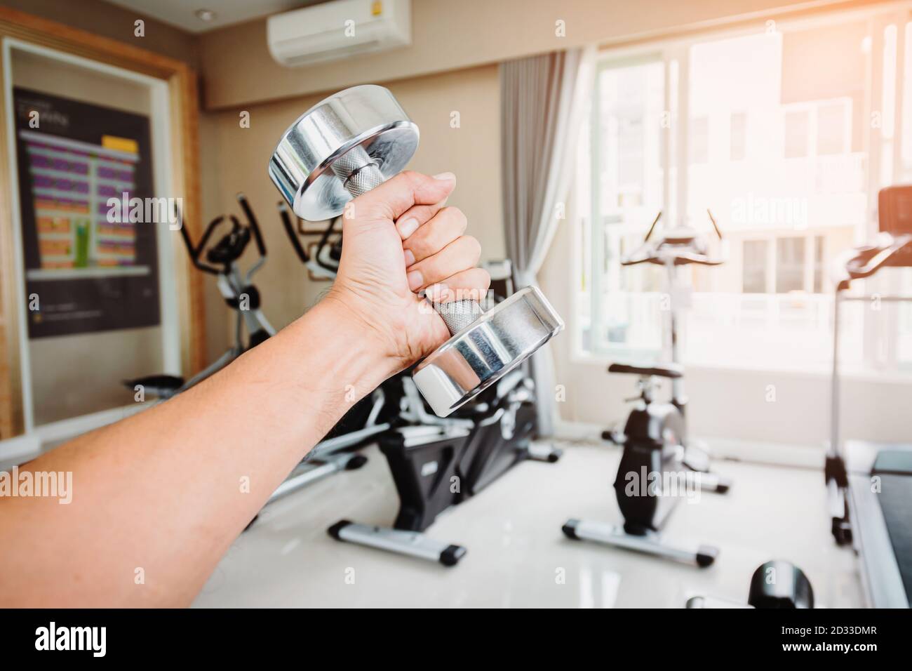 Closeup a man's hand holds a dumbbell with his left hand in the gym ...