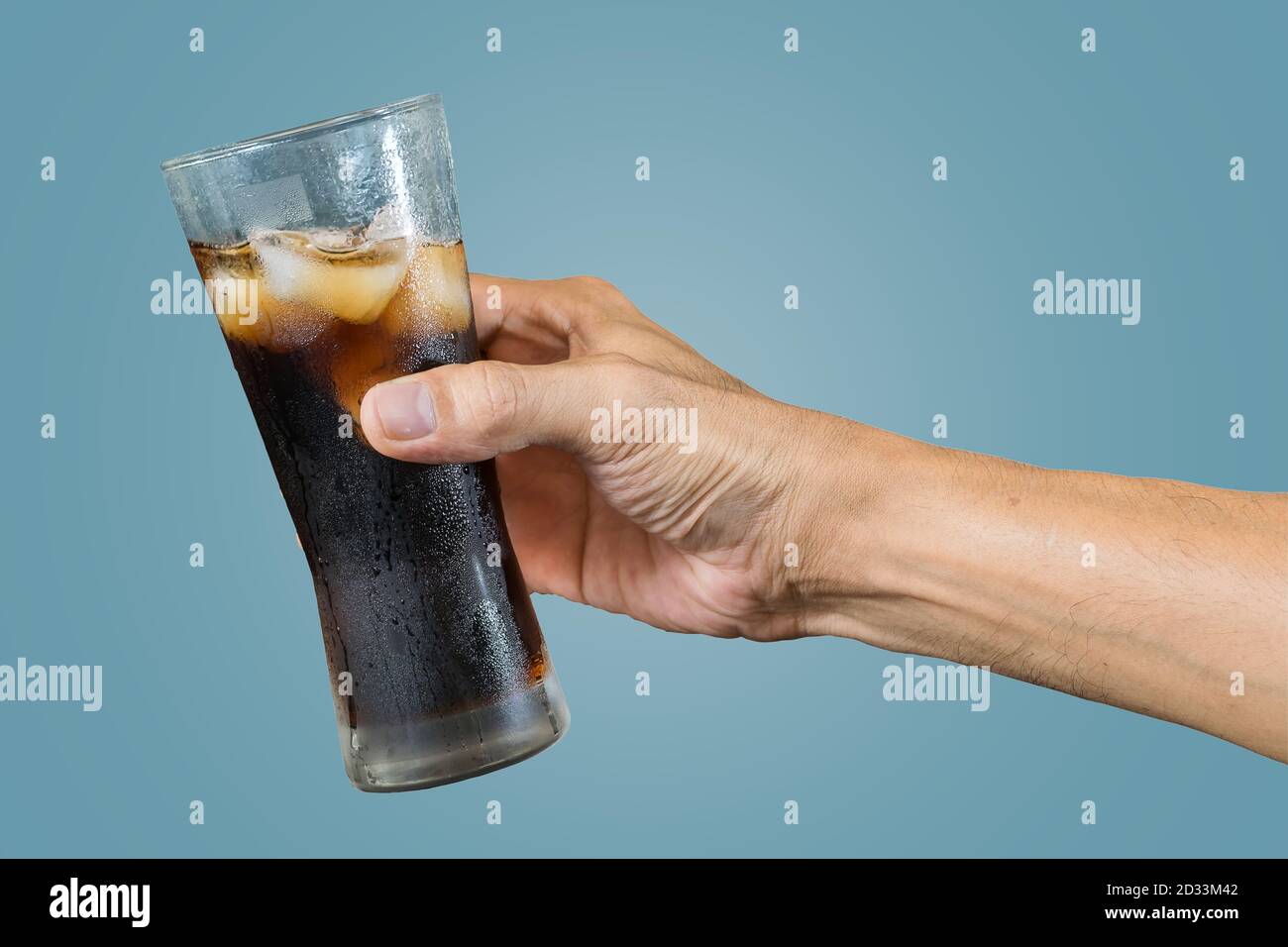 Hand of a man holding a cola glass with ices isolated on pastel color ...