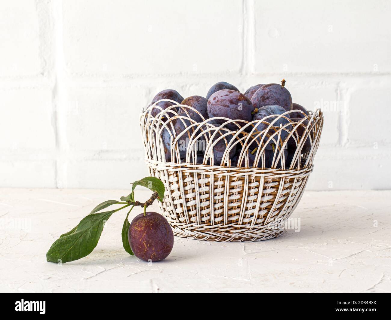 Just picked ripe plums in a wicker basket on the white background. Just ...