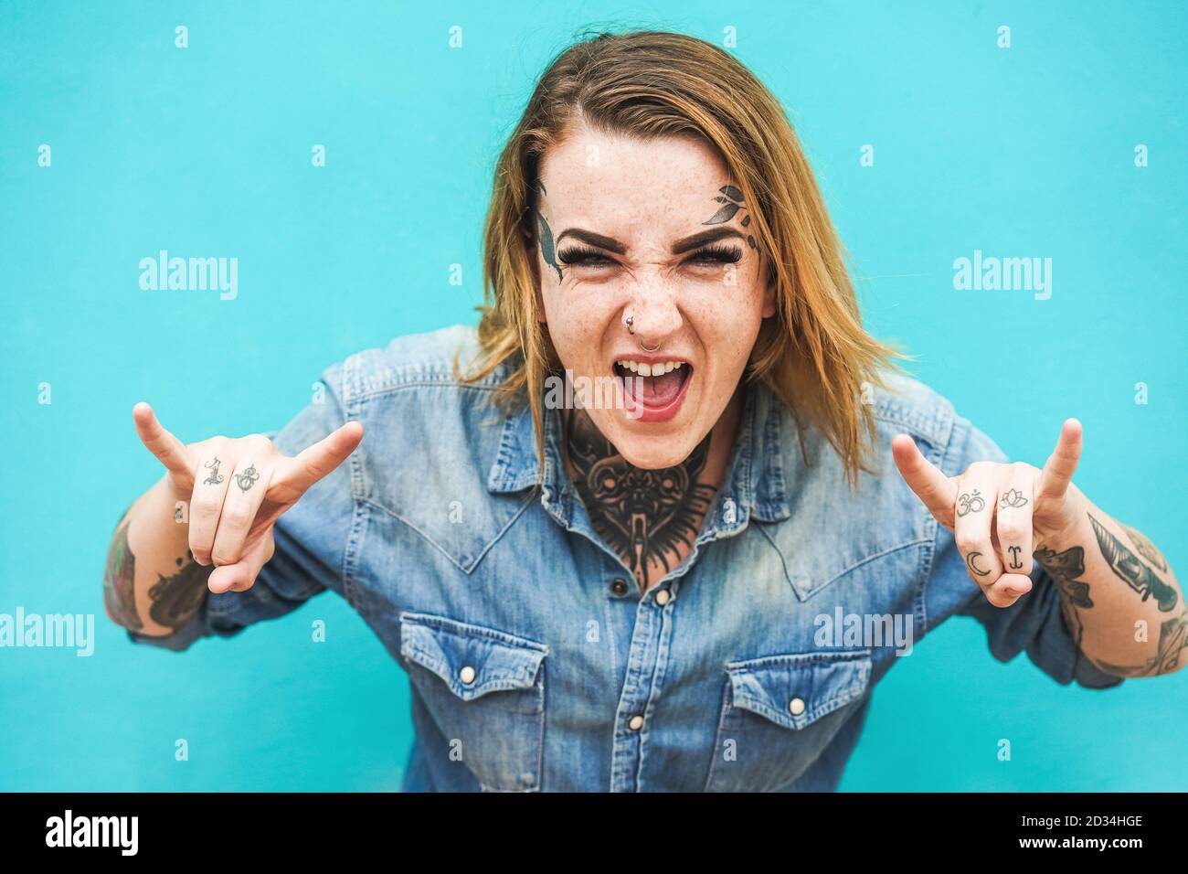 Young woman with tattoos shouting and making rock n roll sign - Focus ...