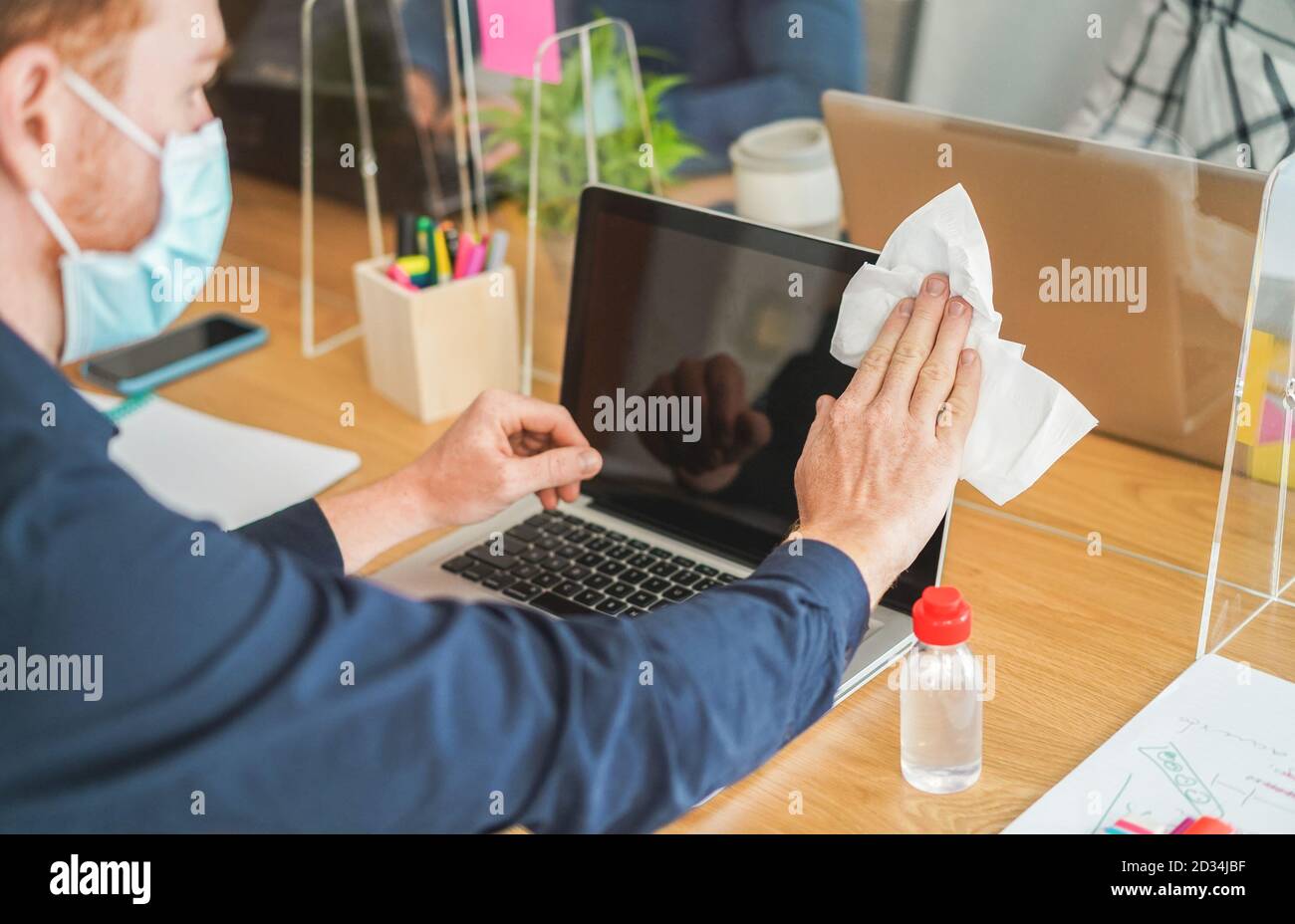 Young worker using sanitizer gel to disinfect his laptop computer ...