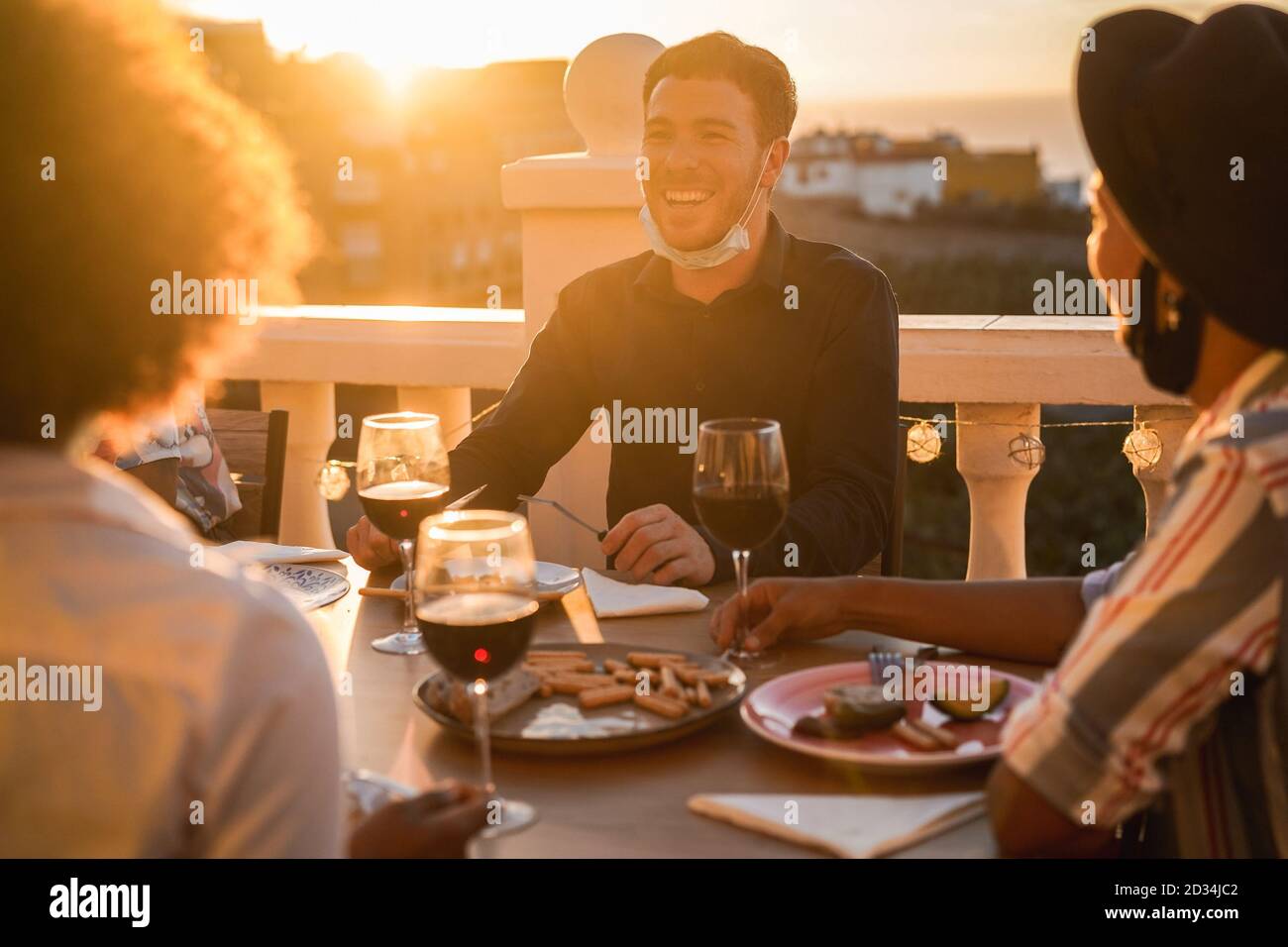 Young multiracial people eating and drinking red wine while wearing ...