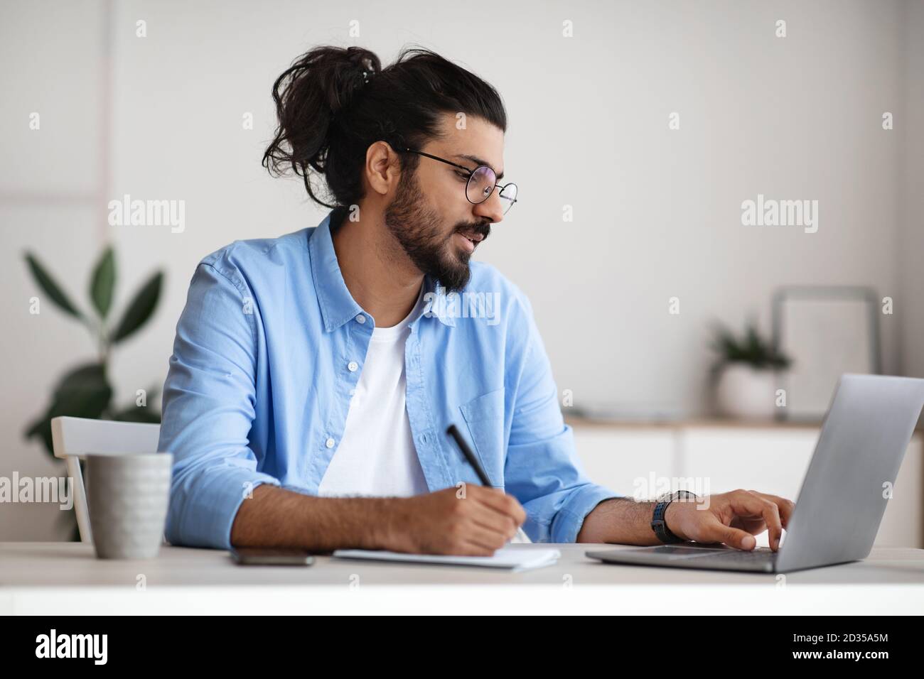 Indian male entrepreneur using laptop and taking notes while working in ...
