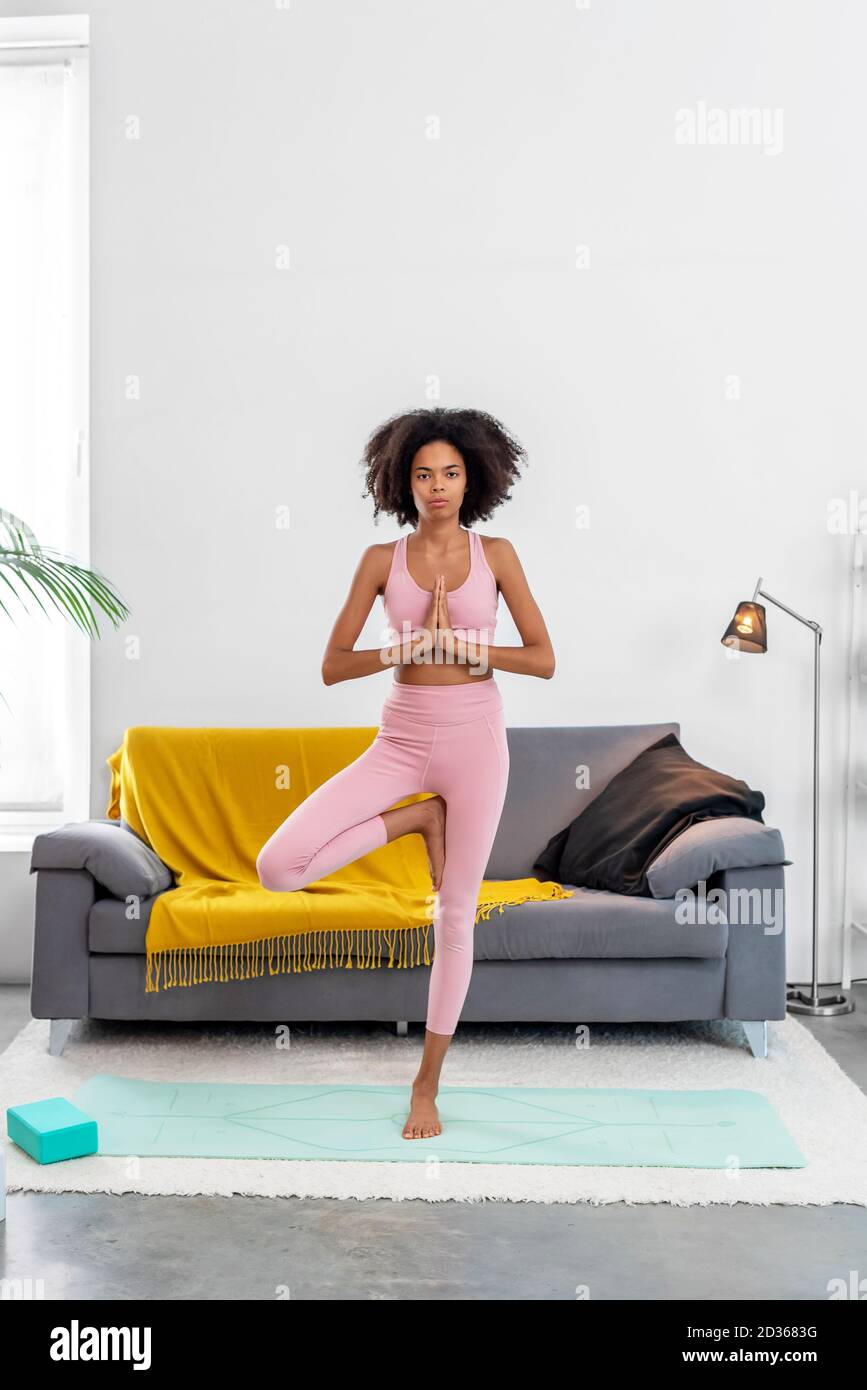 Afroamerican woman practicing yoga tree pose at cozy home Stock Photo ...
