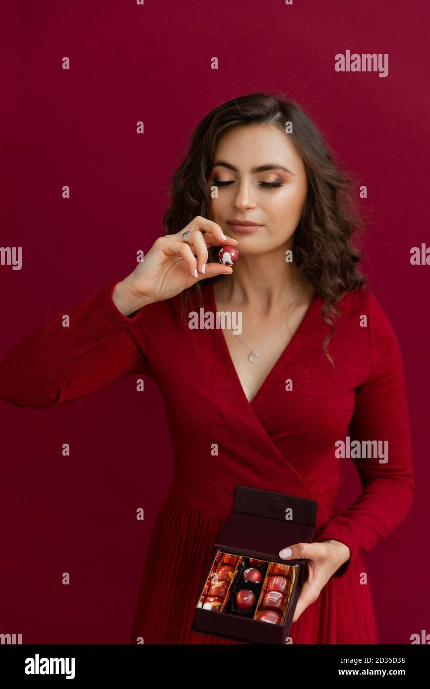 Pretty female holding one round chocolate candy. Woman in red dress ...