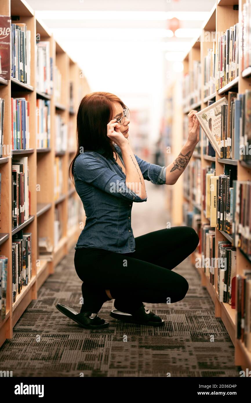 A solitary young woman browsing books at her local library with view of ...