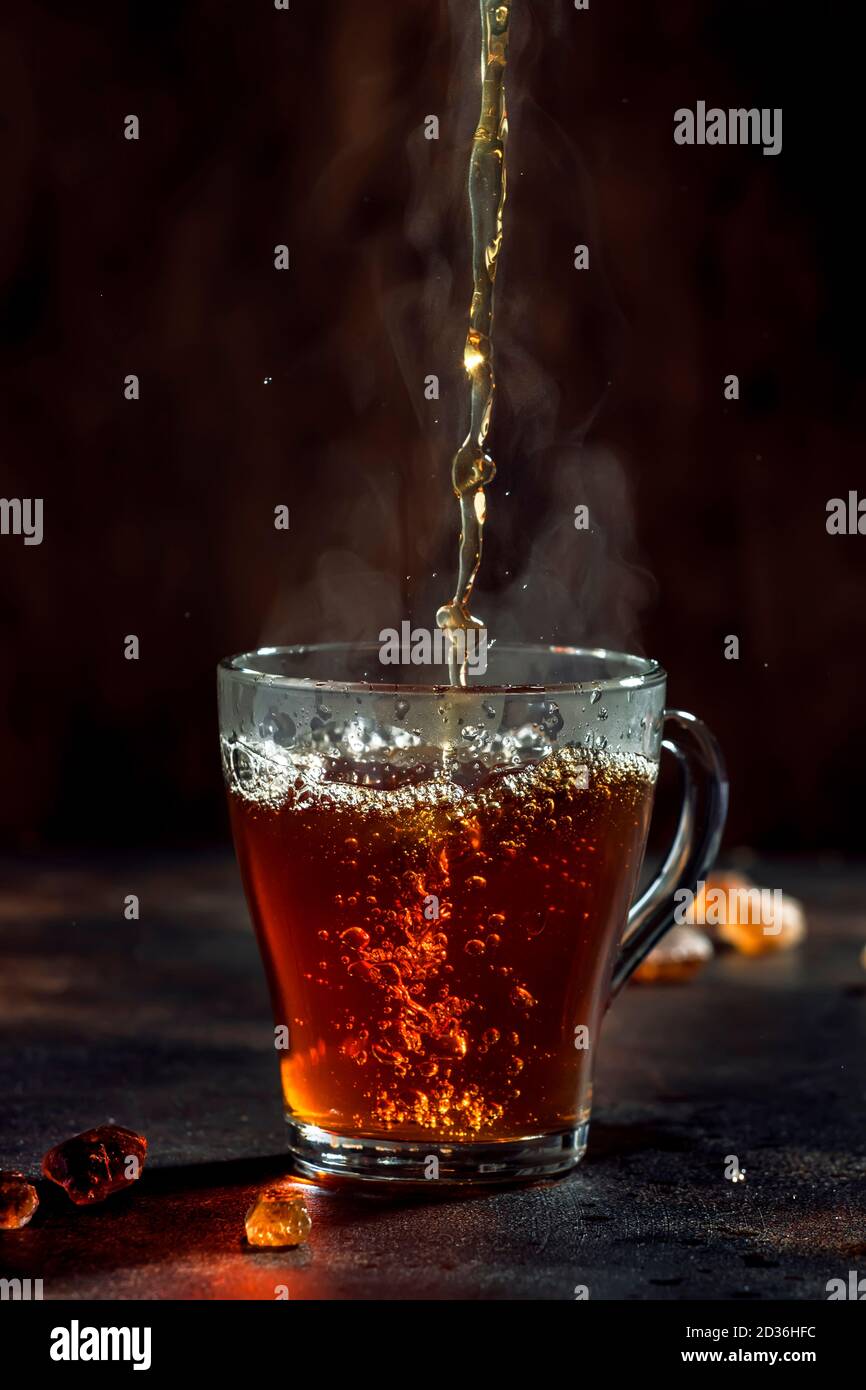 Black tea pouring into glass cup with natural steam on brown background ...