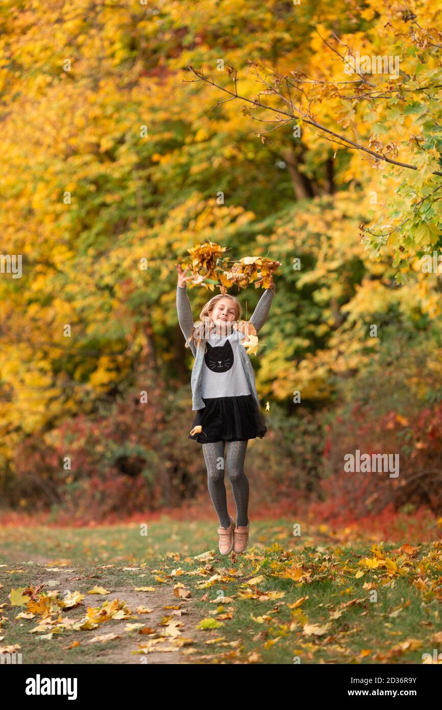 Beautiful little girl jumping with autumn leaves in the park outdoor ...