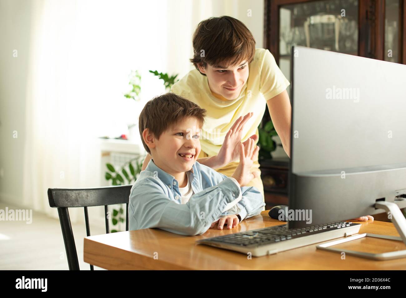 Smiling boy and teenager chatting online and waving at the computer ...