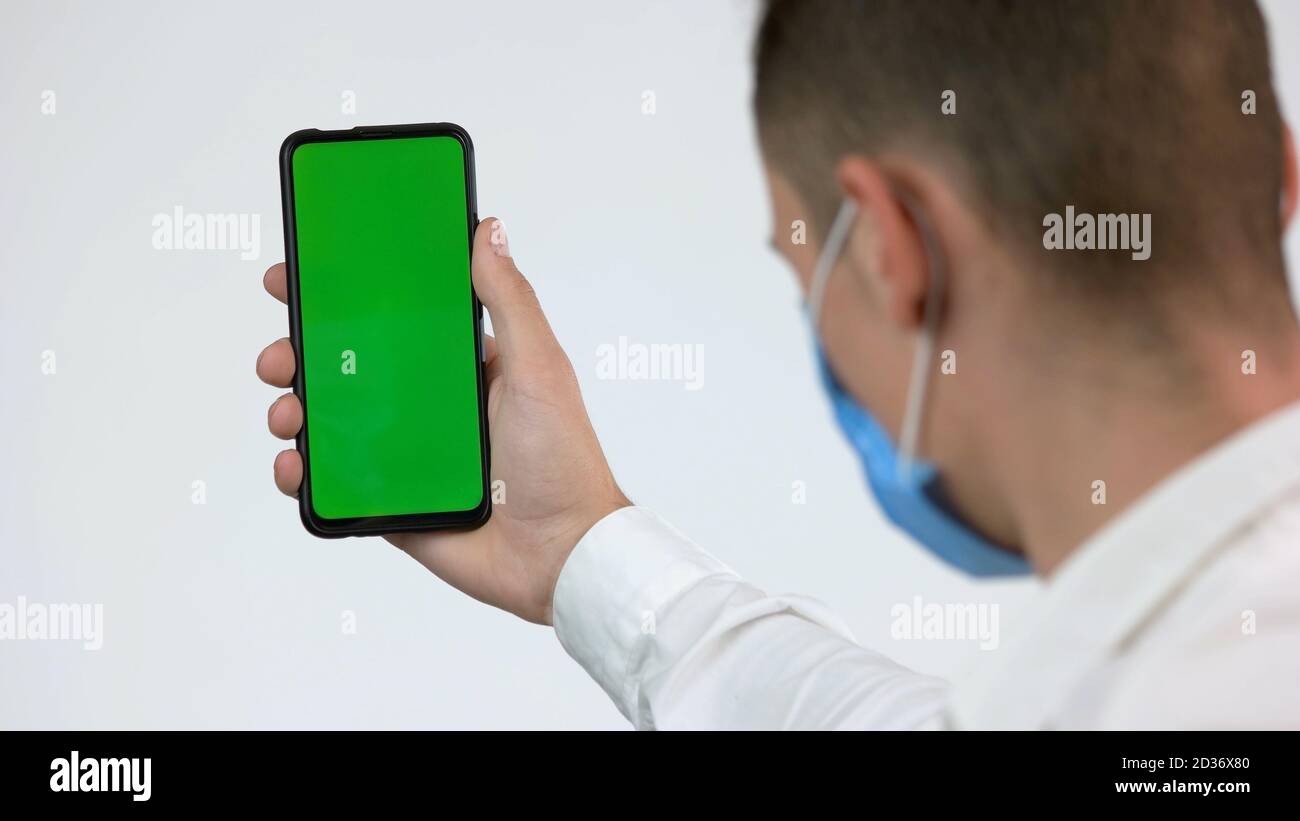 Man in face mask looks at green phone screen Stock Photo - Alamy