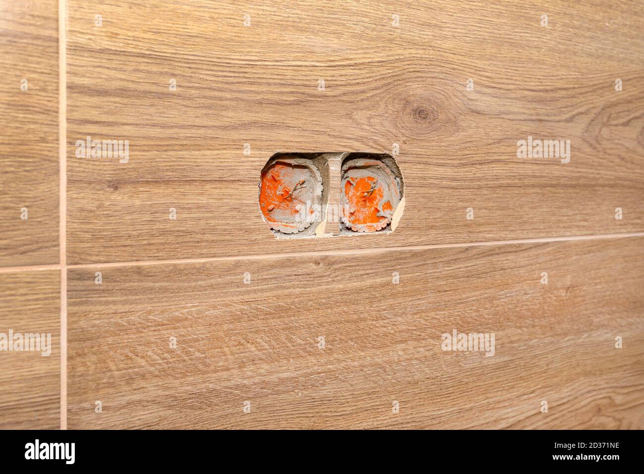 Two electric sockets placed in a wall lined with brown ceramic tiles in ...