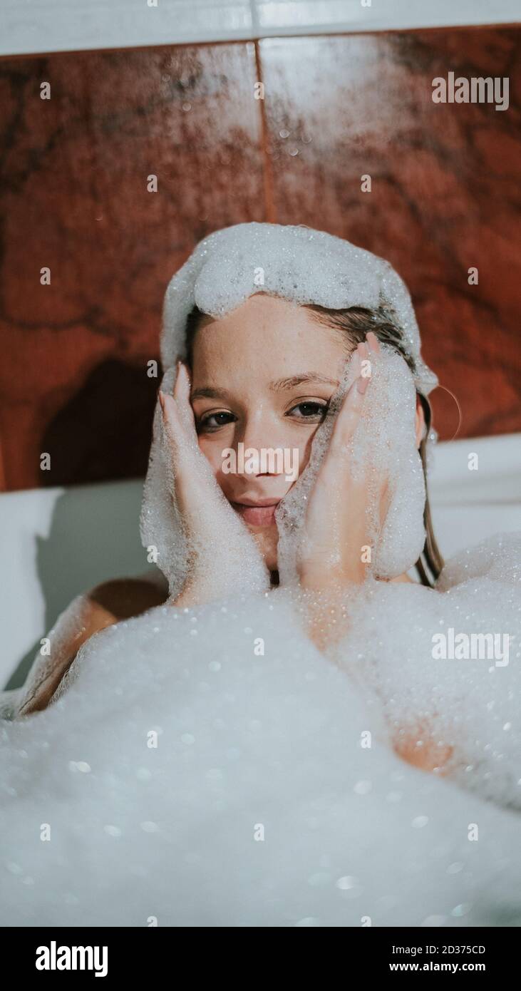 Vertical shot of a beautiful young woman covered in bubbles while ...