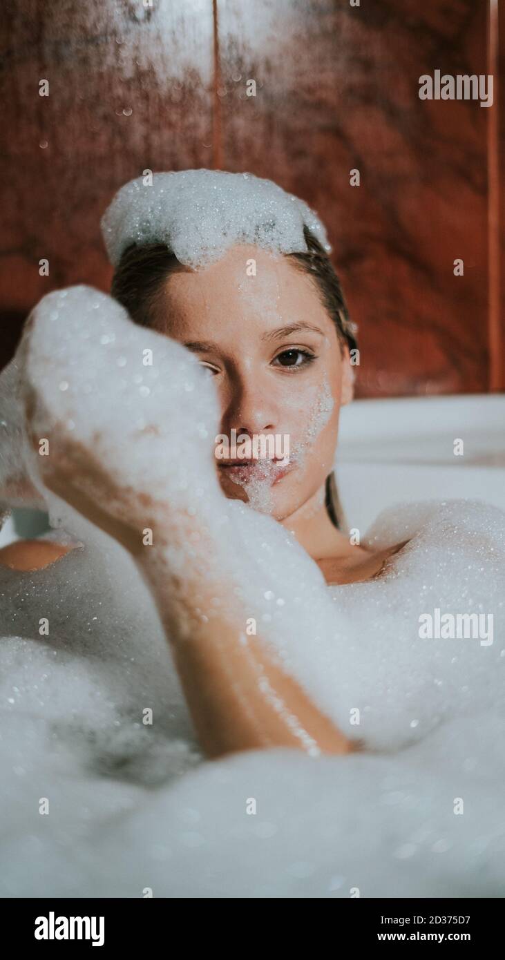 Vertical shot of a beautiful young woman covered in bubbles while ...