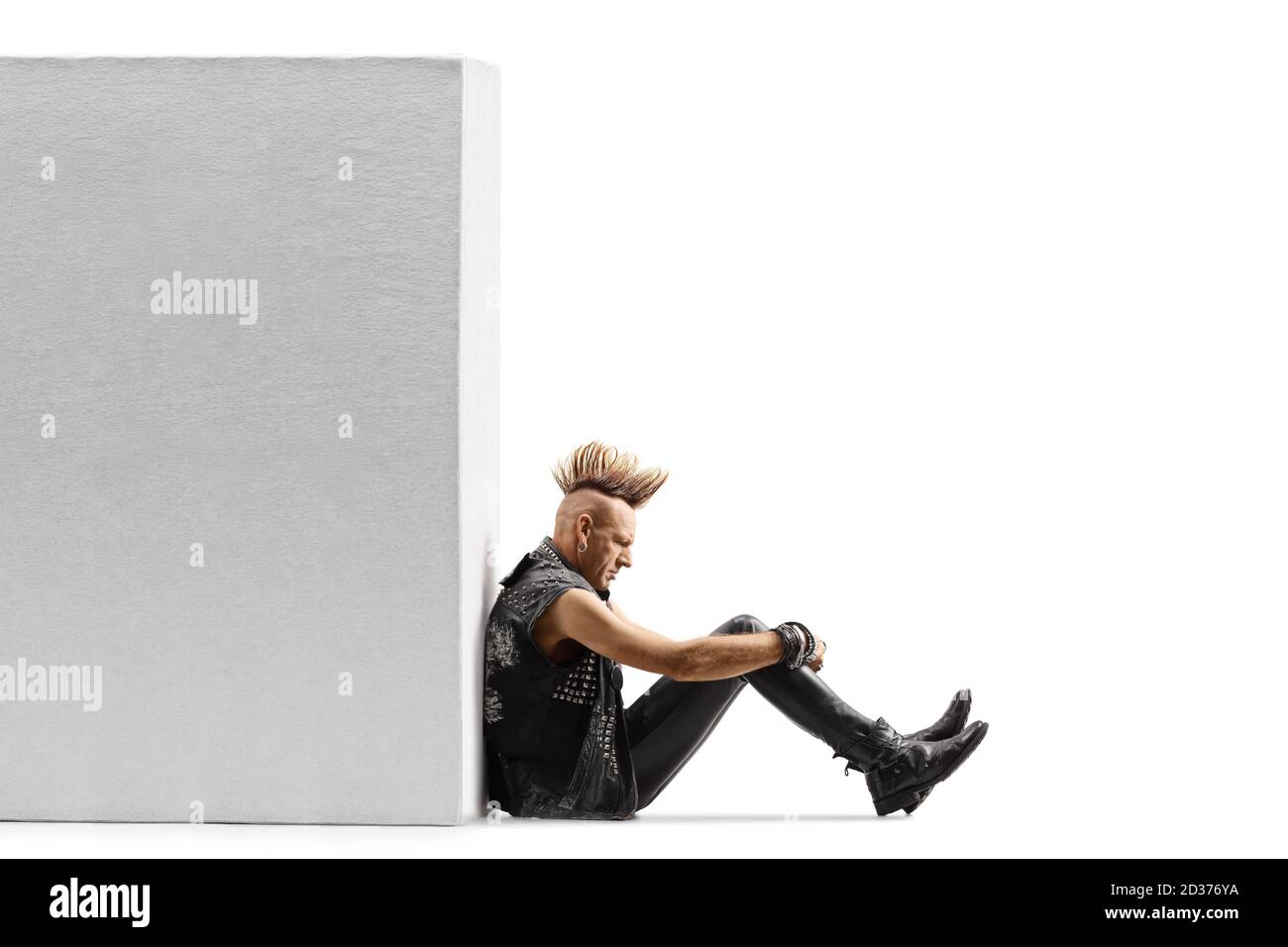 Punk rocker with a mohawk sitting on the ground and leaning on a white ...