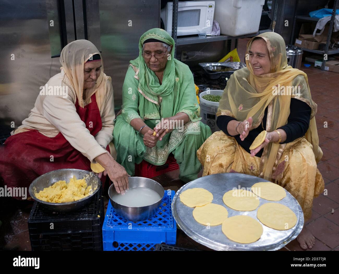 3 older Sikh woman volunteers prepare roti bread in a langar, a ...