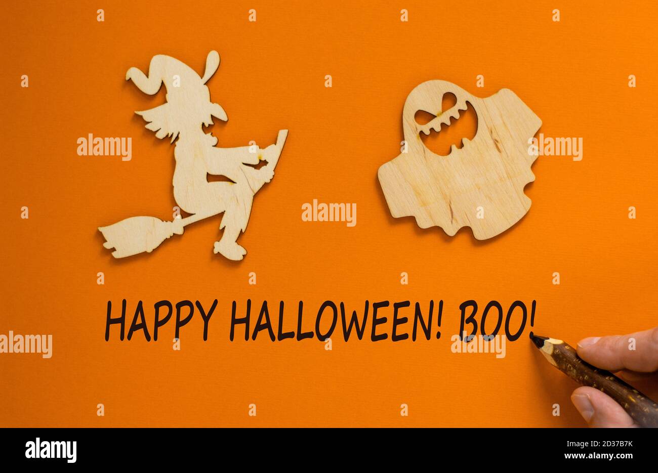 Hand with black pencil writing 'happy halloween, boo'. Wooden witch and ...