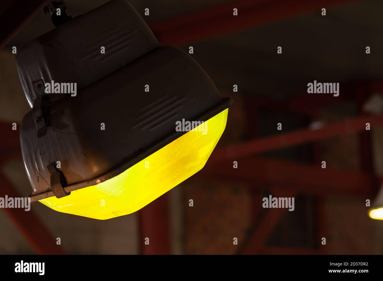 Yellow industrial light mounted on ceiling glowing in dark interior ...