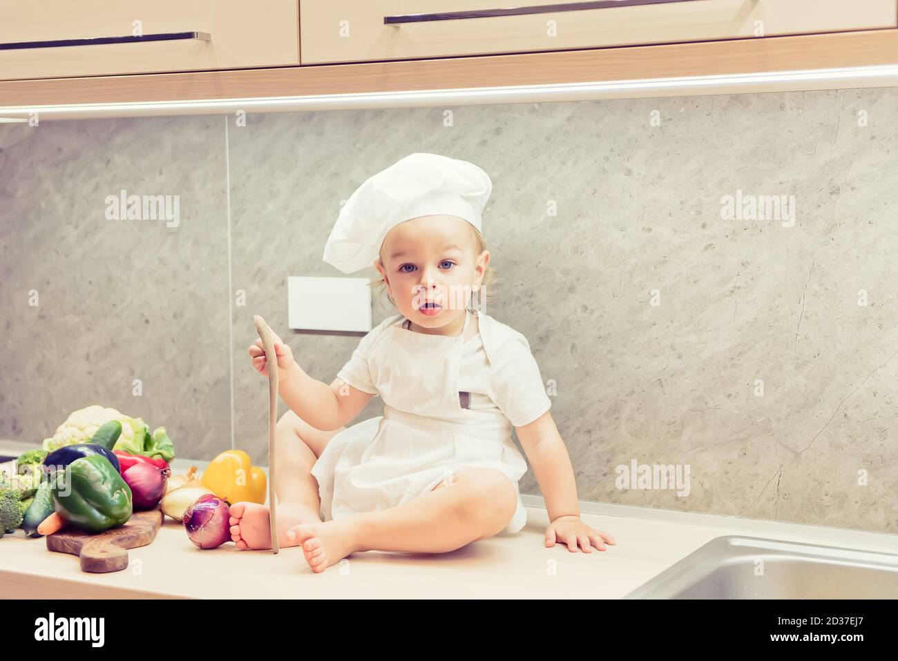 Baby boy sitting among vegetables in the kitchen and prepares for ...