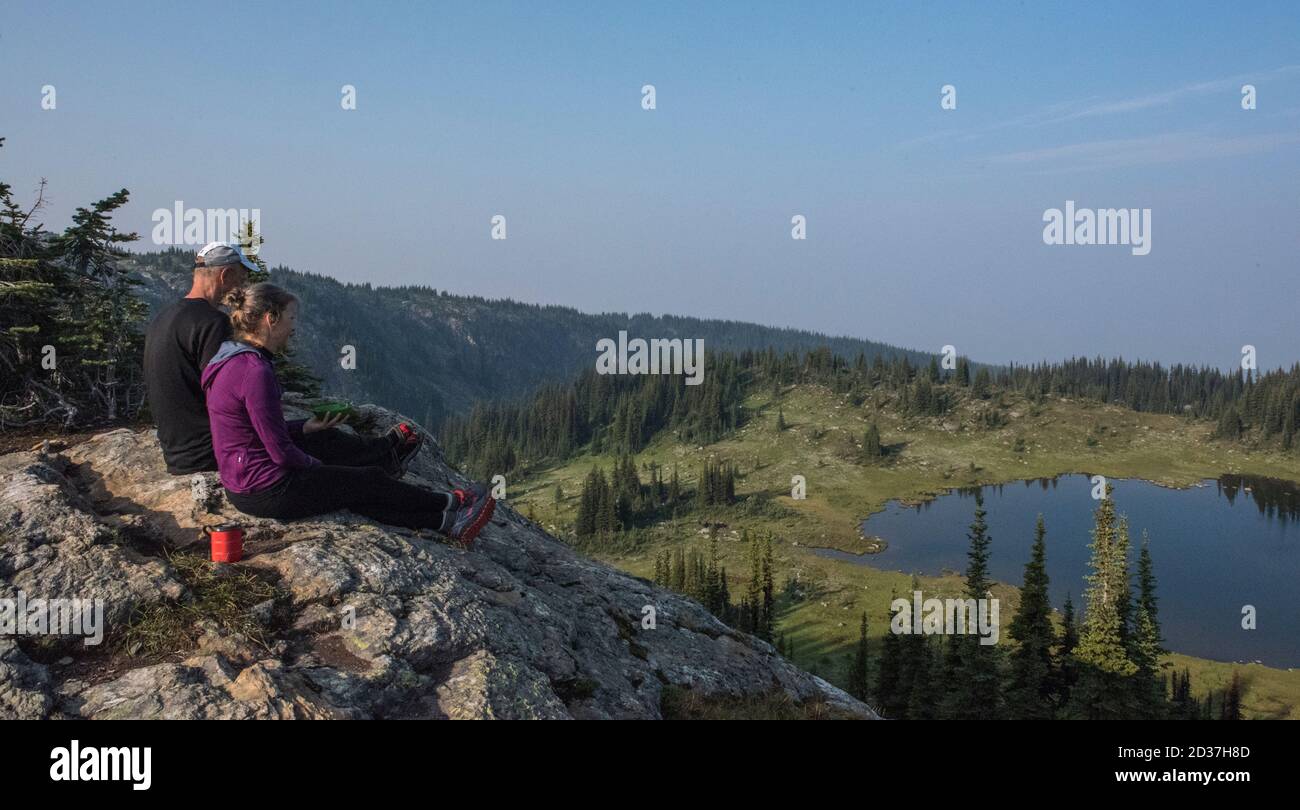Adult couple sitting at top of mountain, over looking lake and valley ...