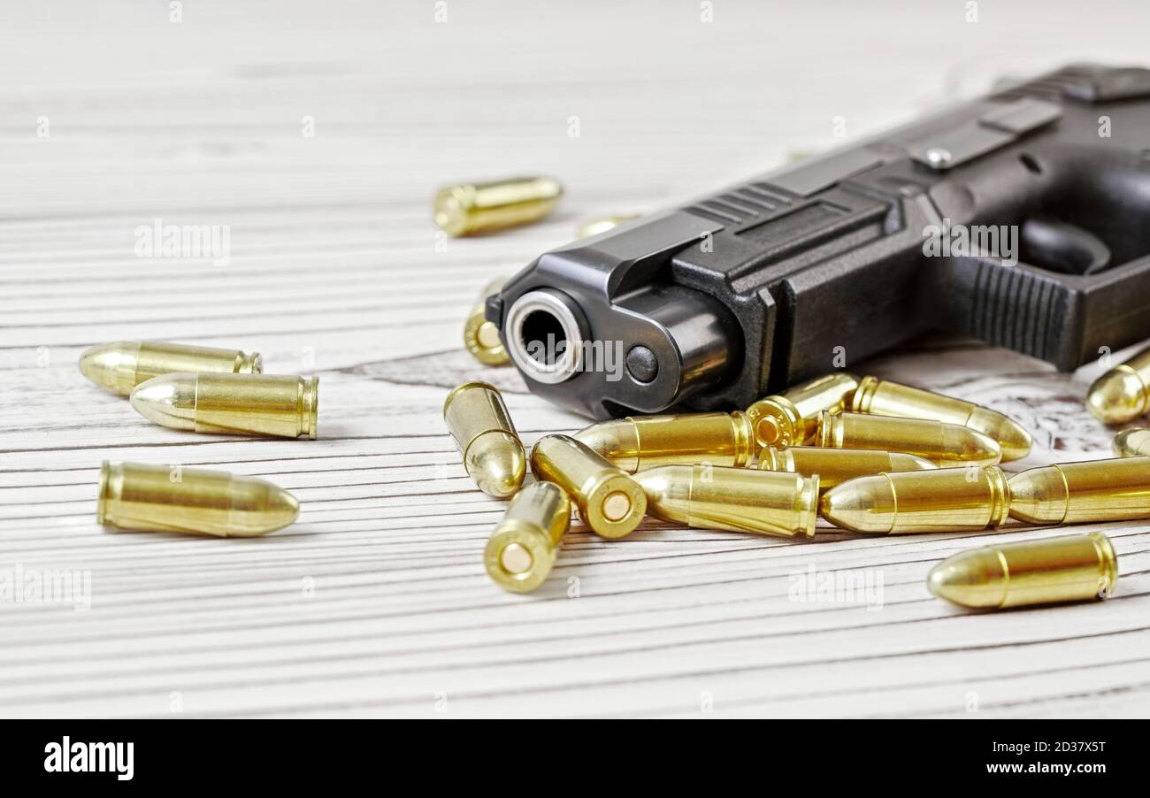 Closeup of modern dark gray gun with yellow brass bullets next to it on ...